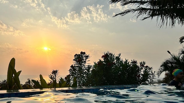 Uma piscina com vista para o pôr do sol, rodeada por plantas tropicais.