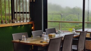 Uma área de refeições com mesa posta para quatro, cadeiras, balcão bar e uma parede verde, com vista através de amplas janelas.