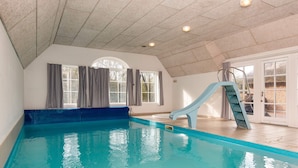 Piscina interna com escorregador, teto azulejado e amplas janelas com cortinas.