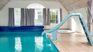 Piscina interna com um escorregador azul, claraboia e vista para árvores lá fora.