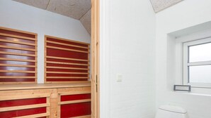 Casa de banho com sanita branca, cabine de duche com ripas de madeira e janela.