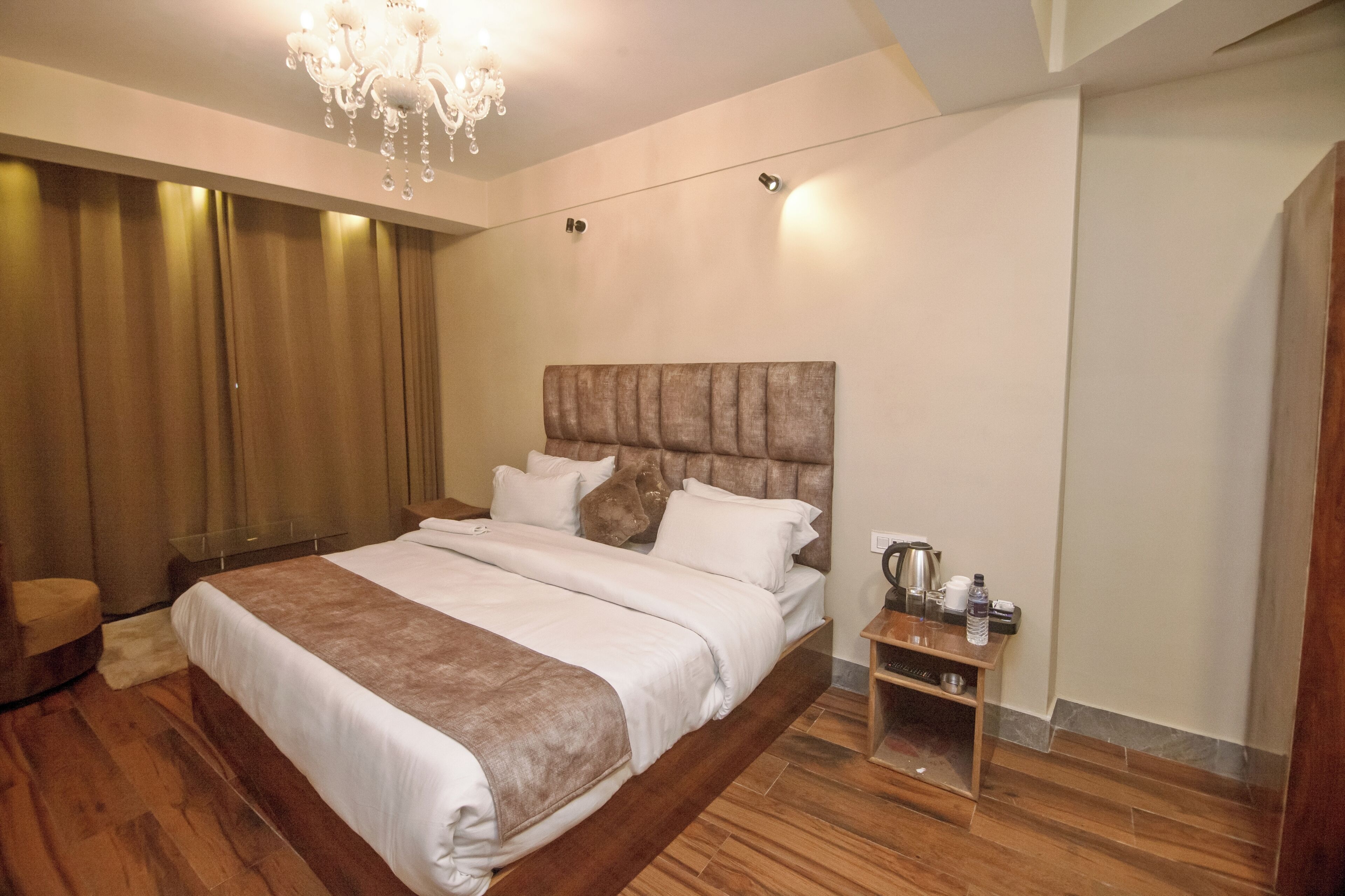 Quarto de hotel moderno com uma cama grande, piso de madeira, um lustre e uma mesa de cabeceira com uma cafeteira.