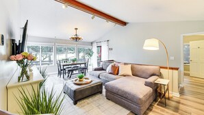 Uma sala de estar ampla com um sofá cinza, uma mesa de centro e uma área de jantar com mesa e cadeiras.