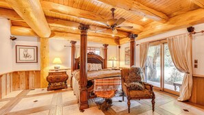 Um quarto espaçoso com uma cama grande, teto de madeira e vista para o exterior por grandes janelas.