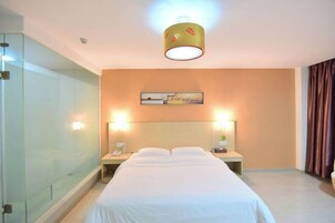 Quarto de hotel com cama, mesas de cabeceira, um quadro na parede e cabine de chuveiro em vidro.