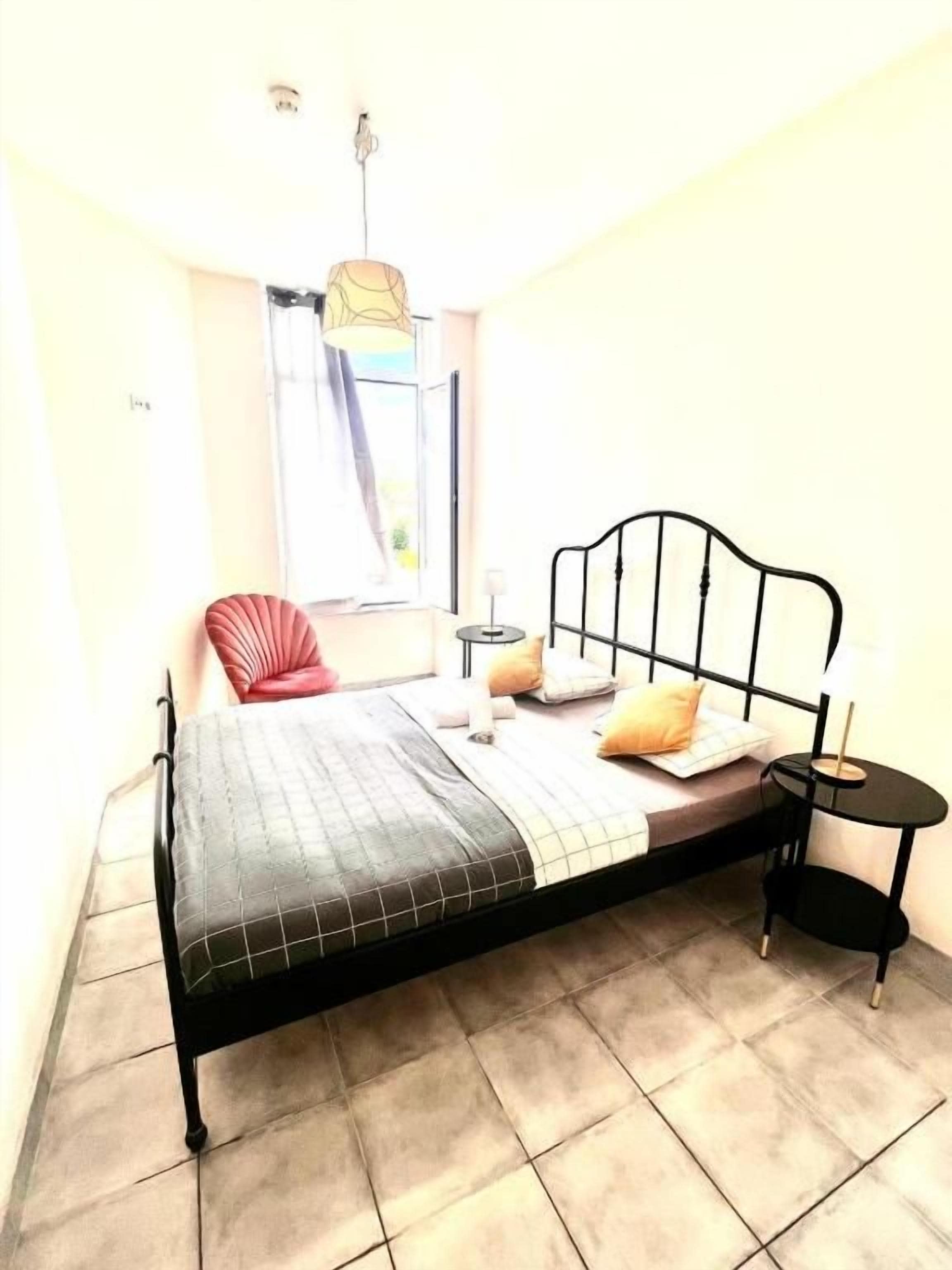 Quarto com cama, cadeira, mesa de cabeceira e janela.