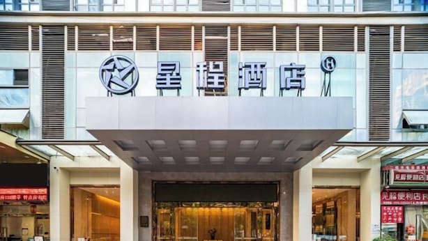 Entrada de hotel com fachada moderna, grandes portas de vidro e área de recepção acolhedora com plantas.