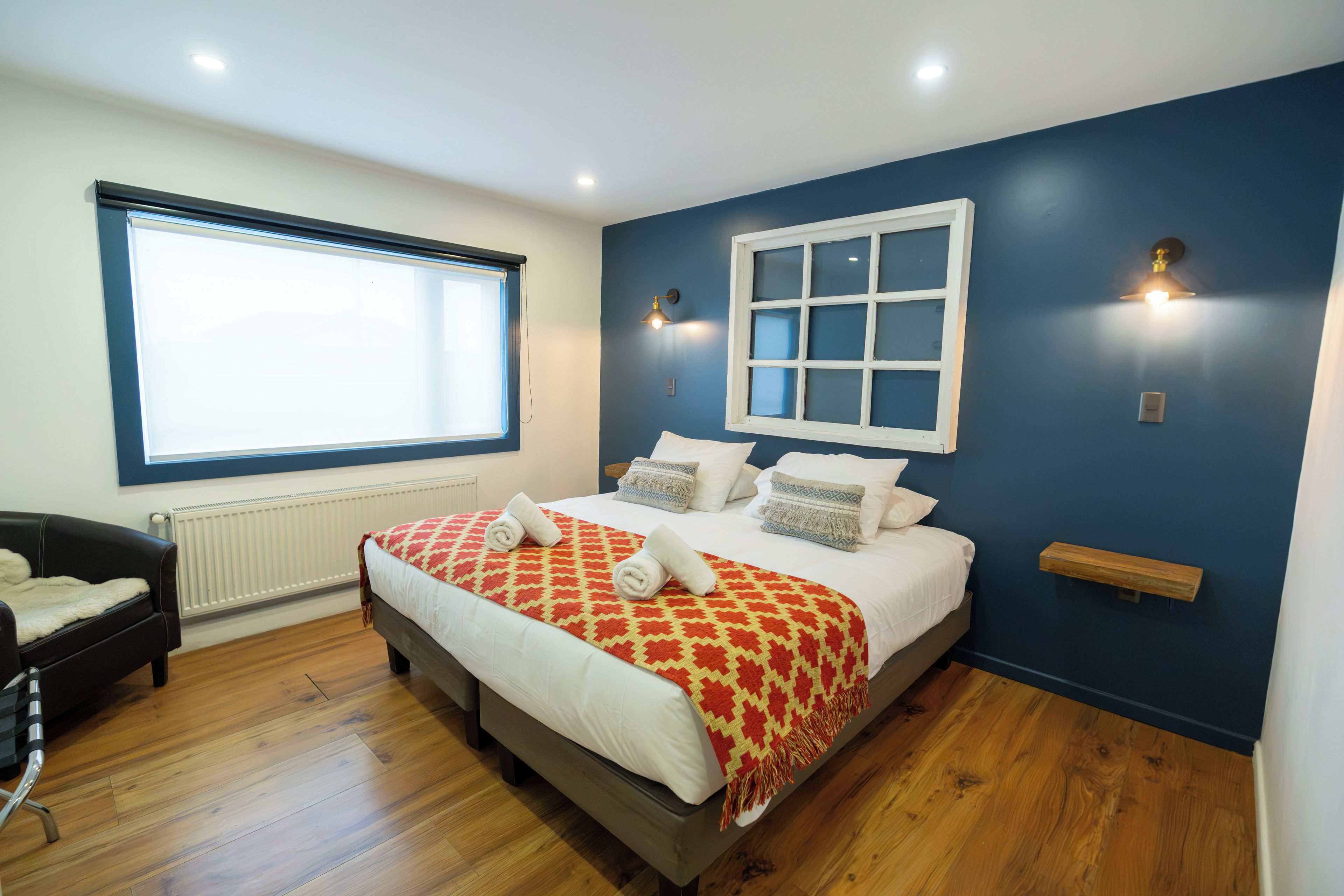 Quarto com cama, cadeira, janela e luminária fixada na parede.