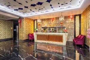Um saguão de hotel com área de bar, balcão de recepção e duas cadeiras vermelhas.