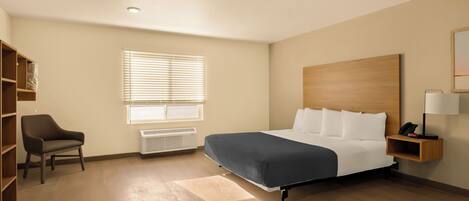 Quarto de hotel com cama, poltrona, mesa de cabeceira, estante de livros e janela com persianas.