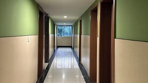 Um corredor comprido e estreito com paredes verde e bege, portas de madeira e chão ladrilhado.