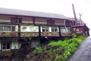 Edifício de vários andares com fachada de pedra, varandas e uma placa com caracteres japoneses.