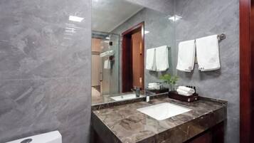 Casa de banho moderna com bancada de mármore, lavatório e um espelho grande. Duas toalhas brancas estão penduradas num porta-toalhas.