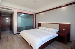 Quarto de hotel moderno com uma cama grande, cabeceira de madeira e uma mesinha de cabeceira.