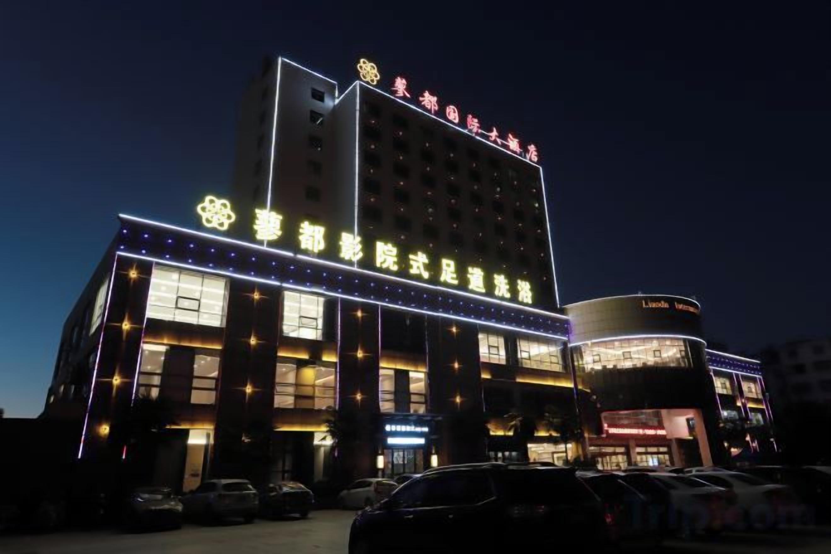 Hotel com vários andares, letreiros iluminados e estacionamento em frente.