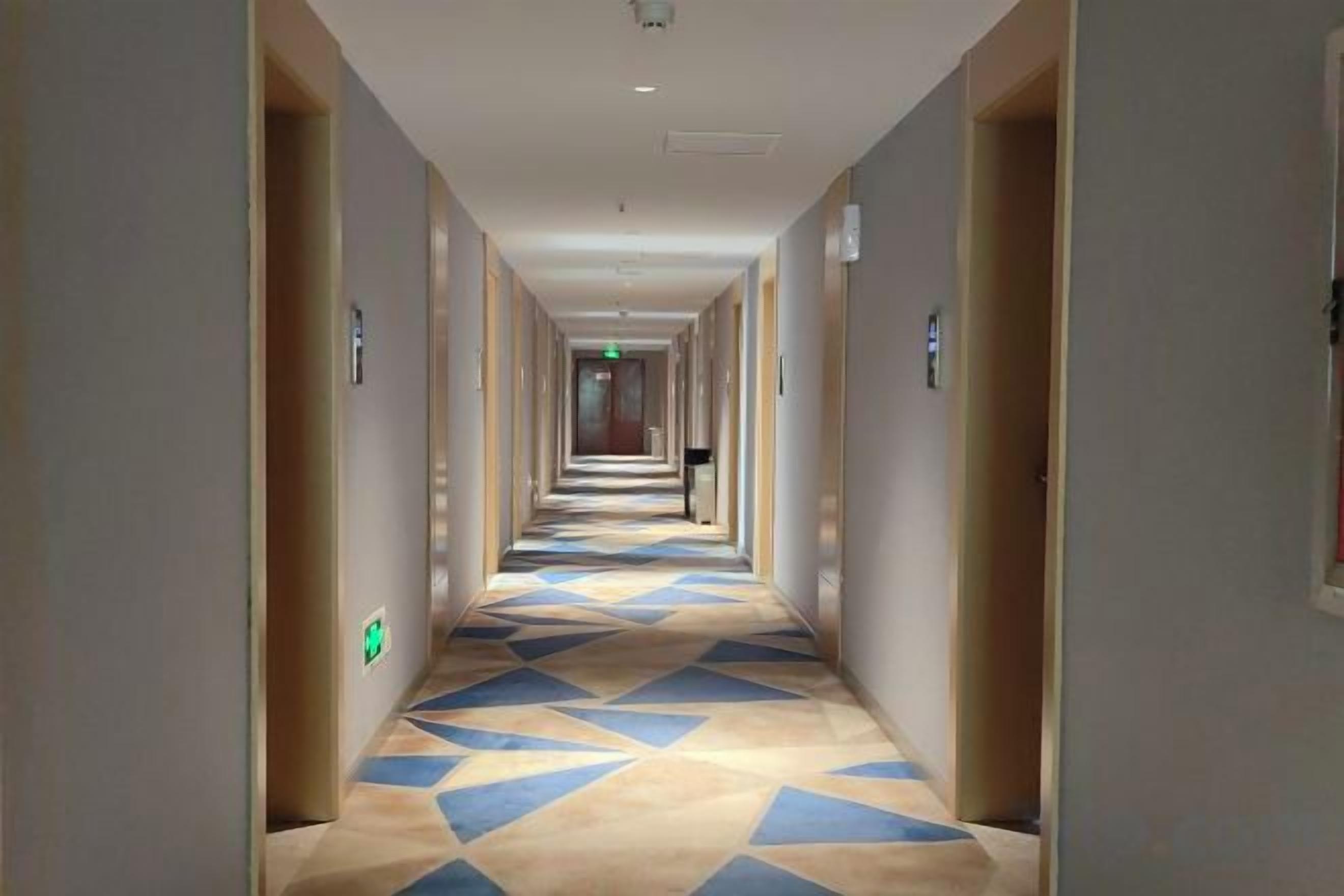 Corredor de hotel com piso estampado, portas de ambos os lados e placa indicando a direção do elevador.