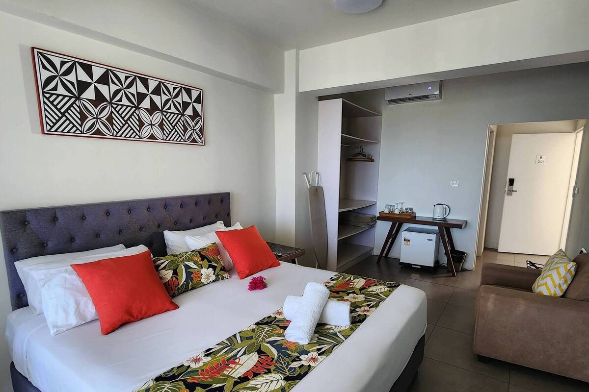 Quarto de hotel com uma cama grande, um sofá, uma escrivaninha com computador e um guarda-roupa.
