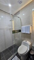 Um banheiro moderno com chuveiro em gabinete de vidro, vaso sanitário e porta-toalhas.