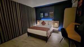 Quarto de hotel moderno com uma cama grande, mesas de cabeceira, uma escrivaninha e uma cadeira.