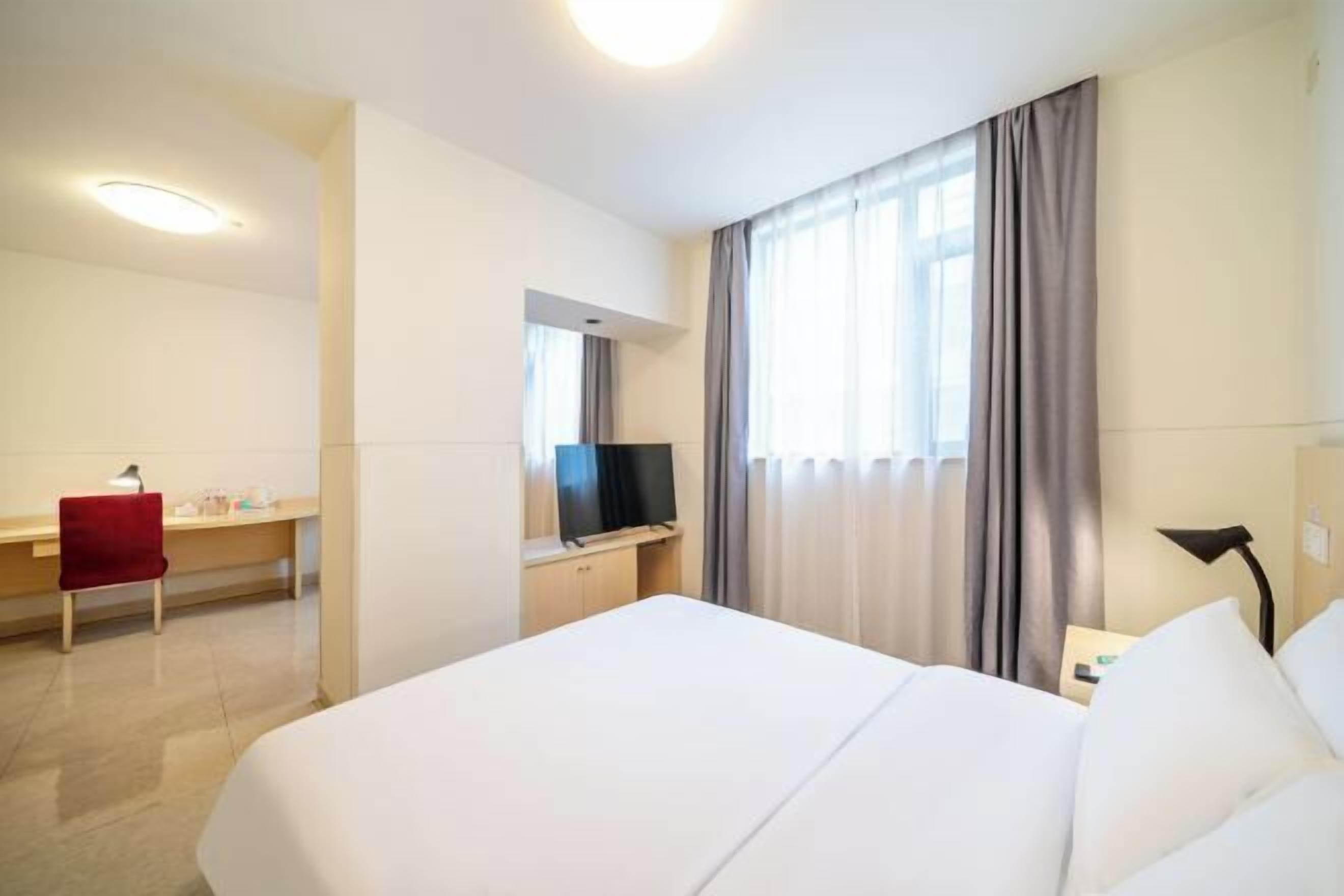 Quarto de hotel com uma cama grande, uma escrivaninha com cadeira, televisão e janela com cortinas.