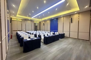 Sala de conferência com fileiras de mesas e cadeiras, equipada com placas de identificação e garrafas de água.