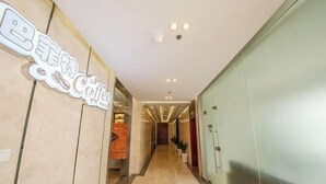 Corredor de hotel com placa de café, área de recepção e uma porta de vidro à direita.