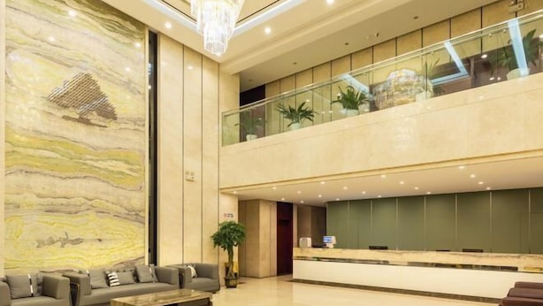 Um hall amplo com parede de mármore, balcão de recepção, sofá e escada.