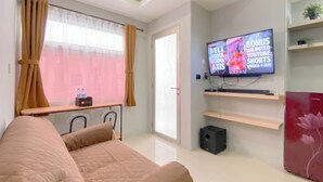 Quarto com cama, televisão na parede, janela com cortinas e pequena escrivaninha com cadeira.