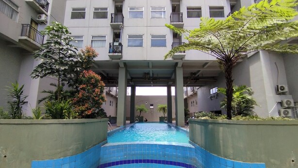 Uma piscina com azulejos azuis, rodeada por vegetação e um edifício com varandas.