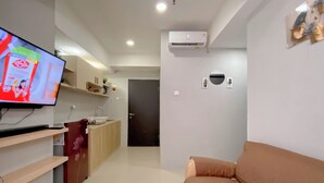 Uma sala de estar moderna com um sofá marrom, uma televisão de tela plana, uma área de cozinha com armários de madeira e um aparelho de ar condicionado na parede.