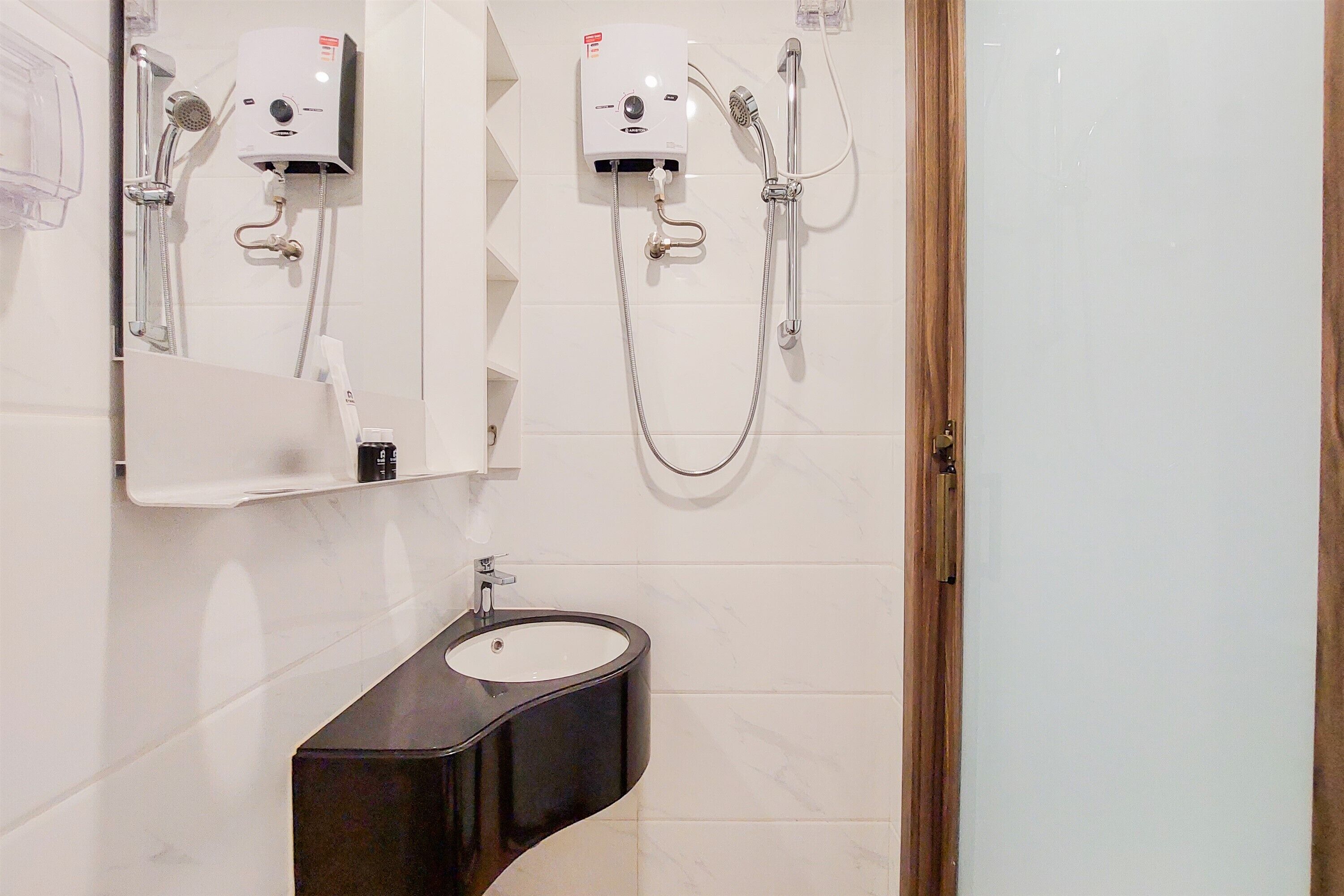 Uma casa de banho moderna com lavatório preto, azulejos brancos, sanita branca e cabine de duche com chuveiro manual.