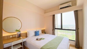 Quarto de hotel com cama, escrivaninha, espelho e janela com vista para a cidade.