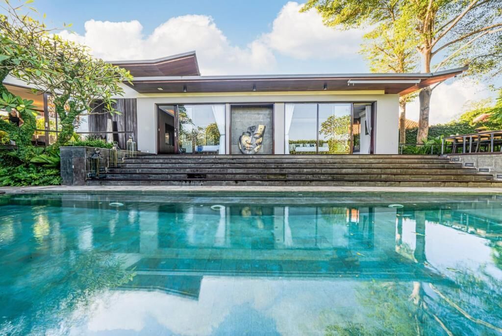 Uma casa moderna com piscina, janelas amplas e escadaria que leva à entrada.