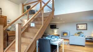 Uma sala de estar moderna com escada de madeira, área de jantar e um espaço de estar aconchegante com lareira.