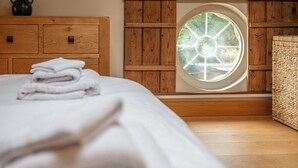 Quarto com cabeceira de madeira, janela redonda com vista e cama bem arrumada com toalhas dobradas.