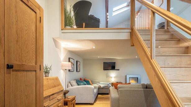 Uma sala de estar moderna em estilo loft, com escada de madeira, conjunto de sofá, televisão de tela plana e lareira.