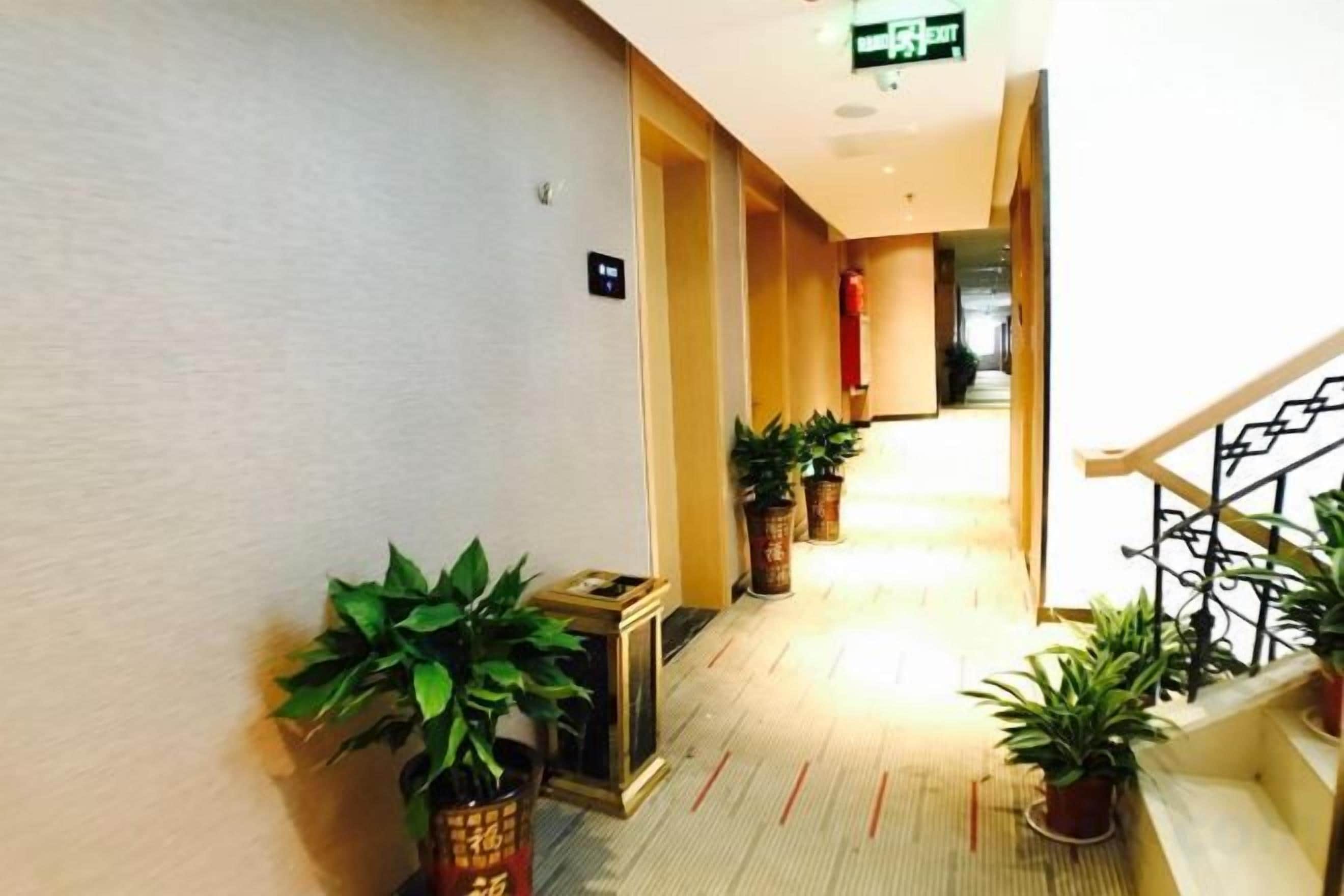 Corredor de hotel com plantas em vasos, extintor de incêndio e escada.