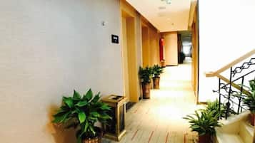 Corredor de hotel com plantas em vasos, extintor de incêndio e escada.