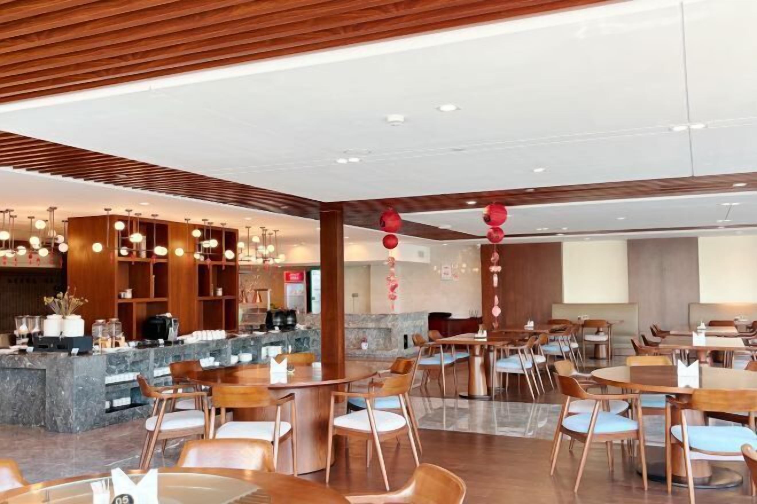 Um restaurante moderno com mesas e cadeiras redondas, um espaço de bar e painéis de teto de madeira.