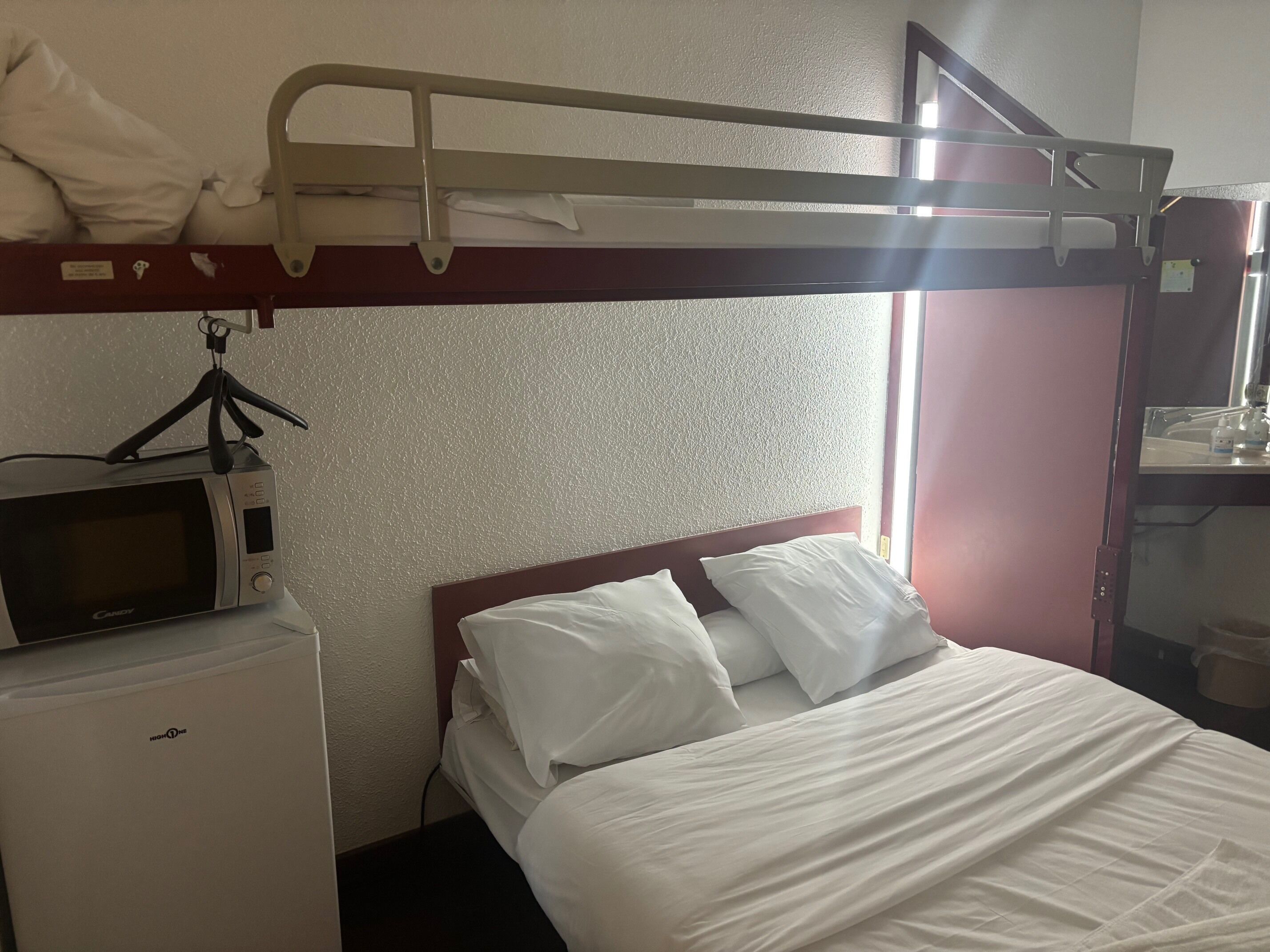 Uma cama beliche com cabeceira, um micro-ondas e um refrigerador pequeno em um quarto de hotel.