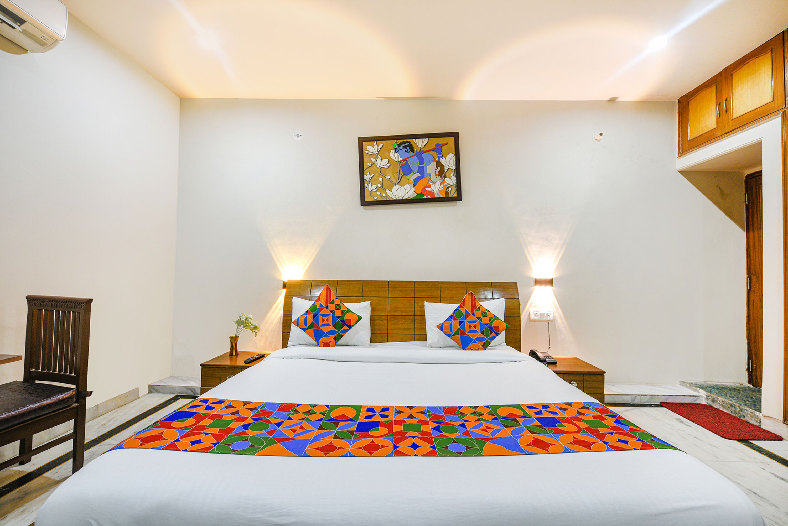 Quarto de hotel com uma cama grande, duas mesas de cabeceira, cabeceira de madeira, uma obra de arte na parede e uma cadeira.