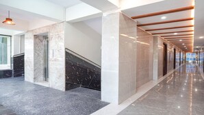 Corredor moderno de hotel com chão de mármore, escada e vigas de madeira no teto.