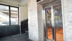 Um elevador com parede de mármore, porta de vidro, painel de teclas e placa indicativa da Kevin Elevators.