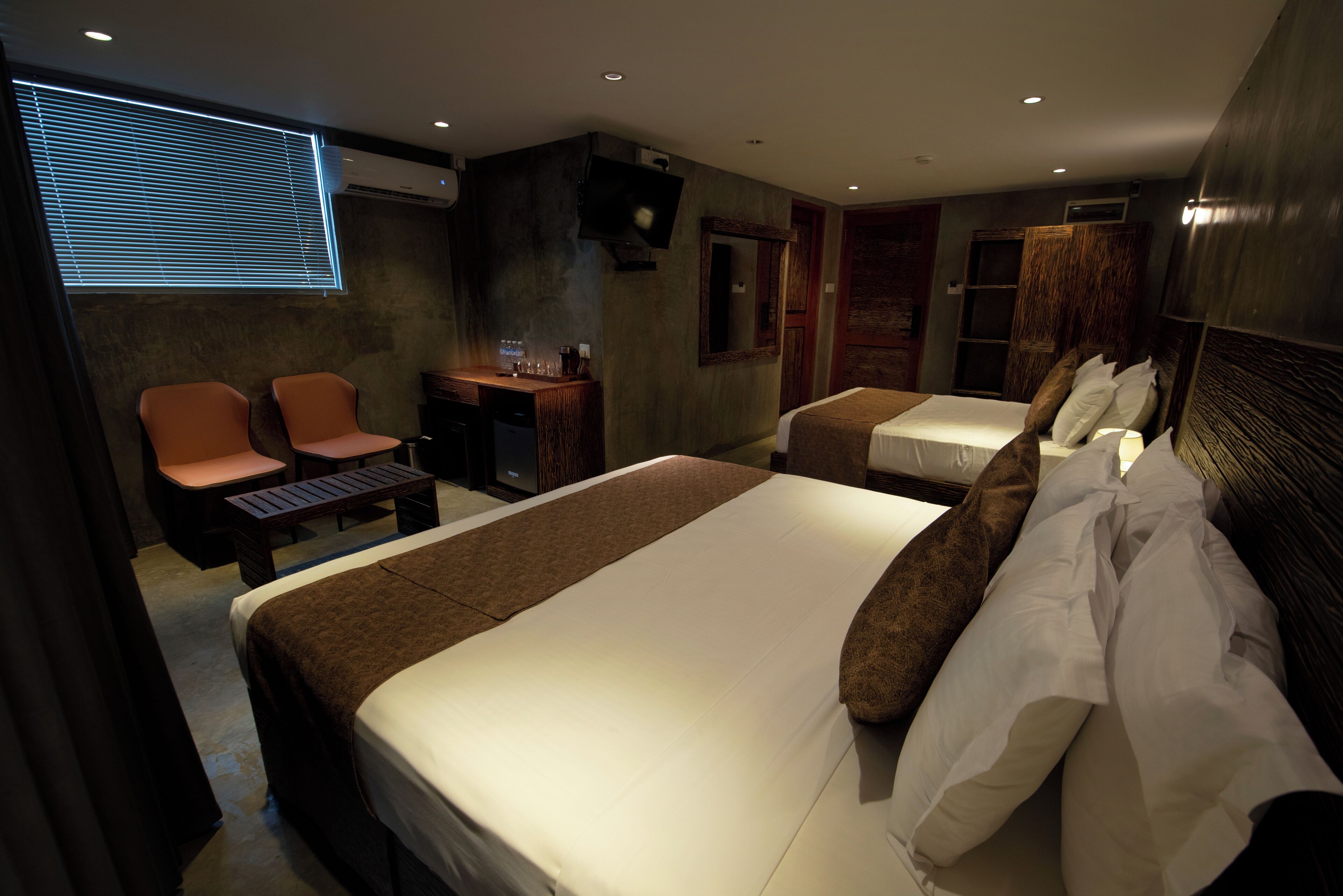 Quarto de hotel com uma cama grande, duas camas menores, uma escrivaninha e duas cadeiras.