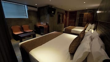 Quarto de hotel com uma cama grande, duas camas menores, uma escrivaninha e duas cadeiras.