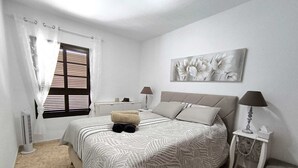 Quarto bem organizado com cama, mesas de cabeceira, luminária e janela com persianas.