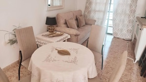 Uma sala de estar acolhedora com sofá, uma mesinha redonda com uma folha decorativa, um abajur e um espelho na parede.