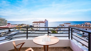 Varanda com mesa e cadeiras, com vista para a costa, edifícios e o mar.