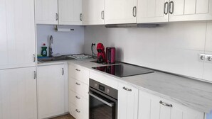 Cozinha moderna com armários brancos, pia de aço inoxidável, cafeteira vermelha e forno embutido.