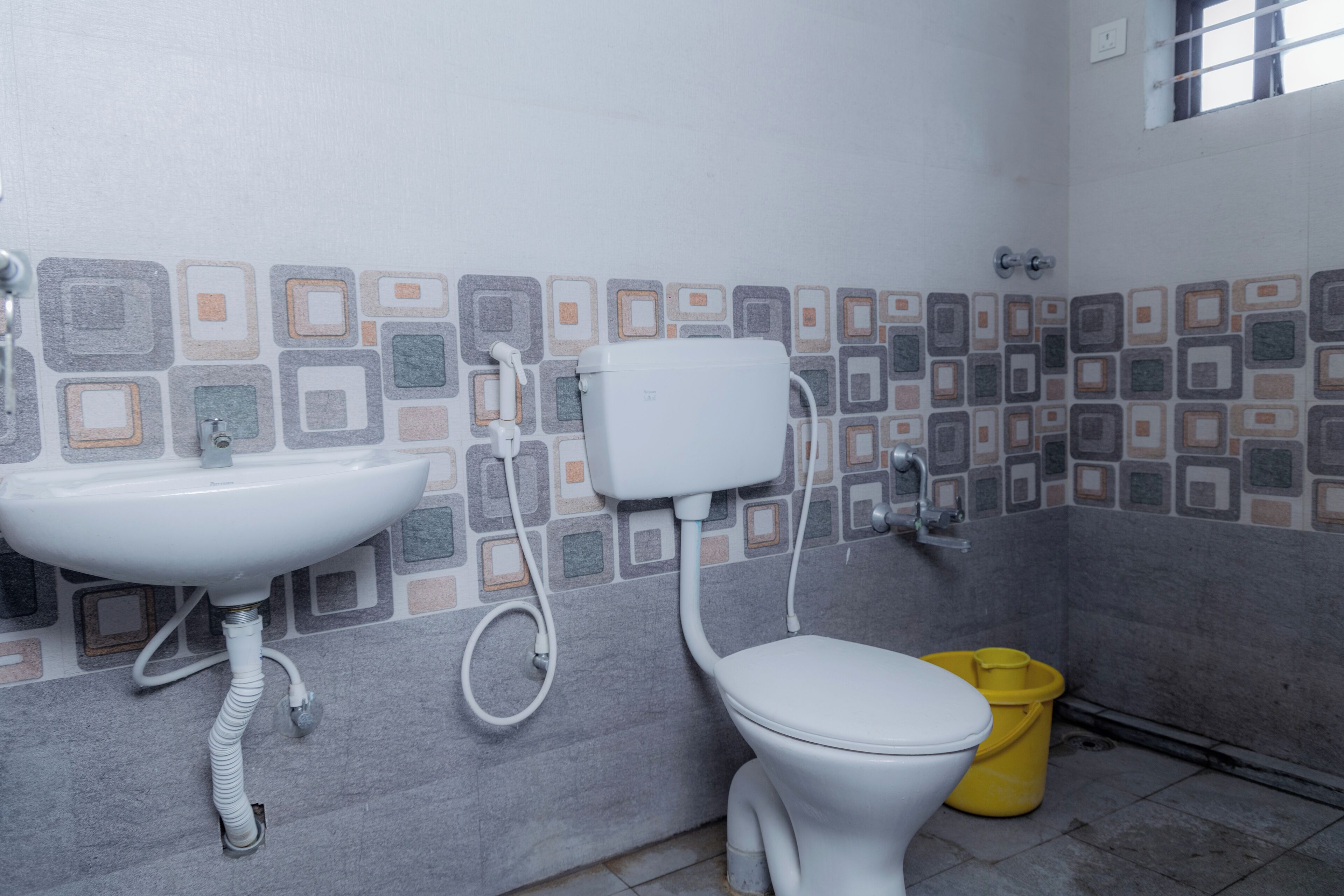 Casa de banho com lavatório branco, sanita e um caixote do lixo amarelo.